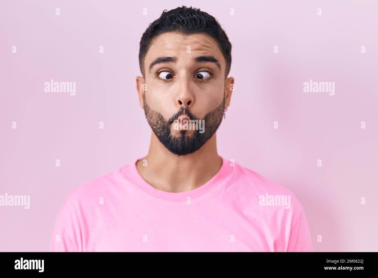 Hispanic young man standing over pink background making fish face with ...