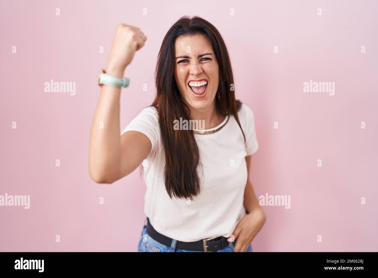 Young brunette woman standing over pink background angry and mad ...