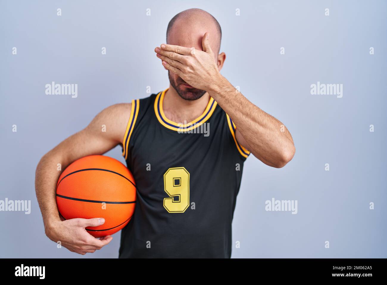 Young bald man with beard wearing basketball uniform holding ball ...