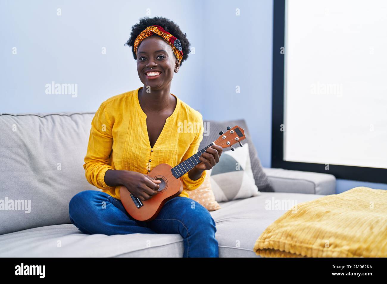 African young woman playing ukulele at home smiling with a happy and ...