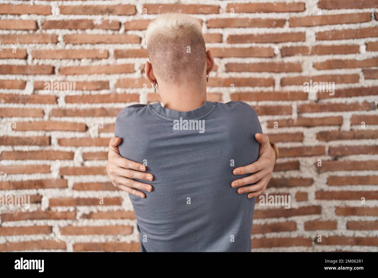 Young caucasian man standing over bricks wall hugging oneself happy and ...
