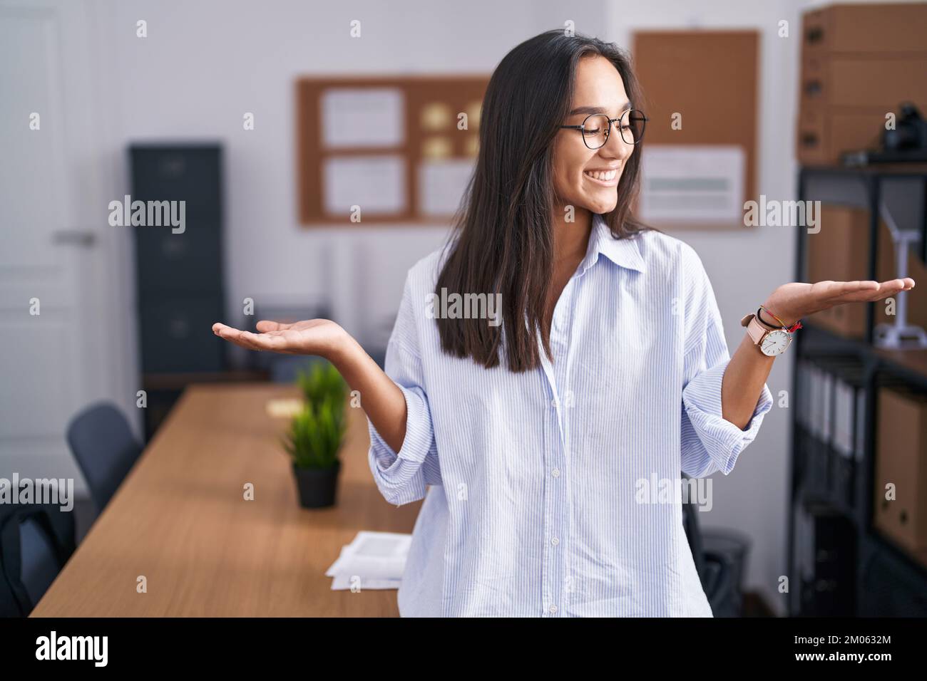 Young hispanic woman at the office smiling showing both hands open ...