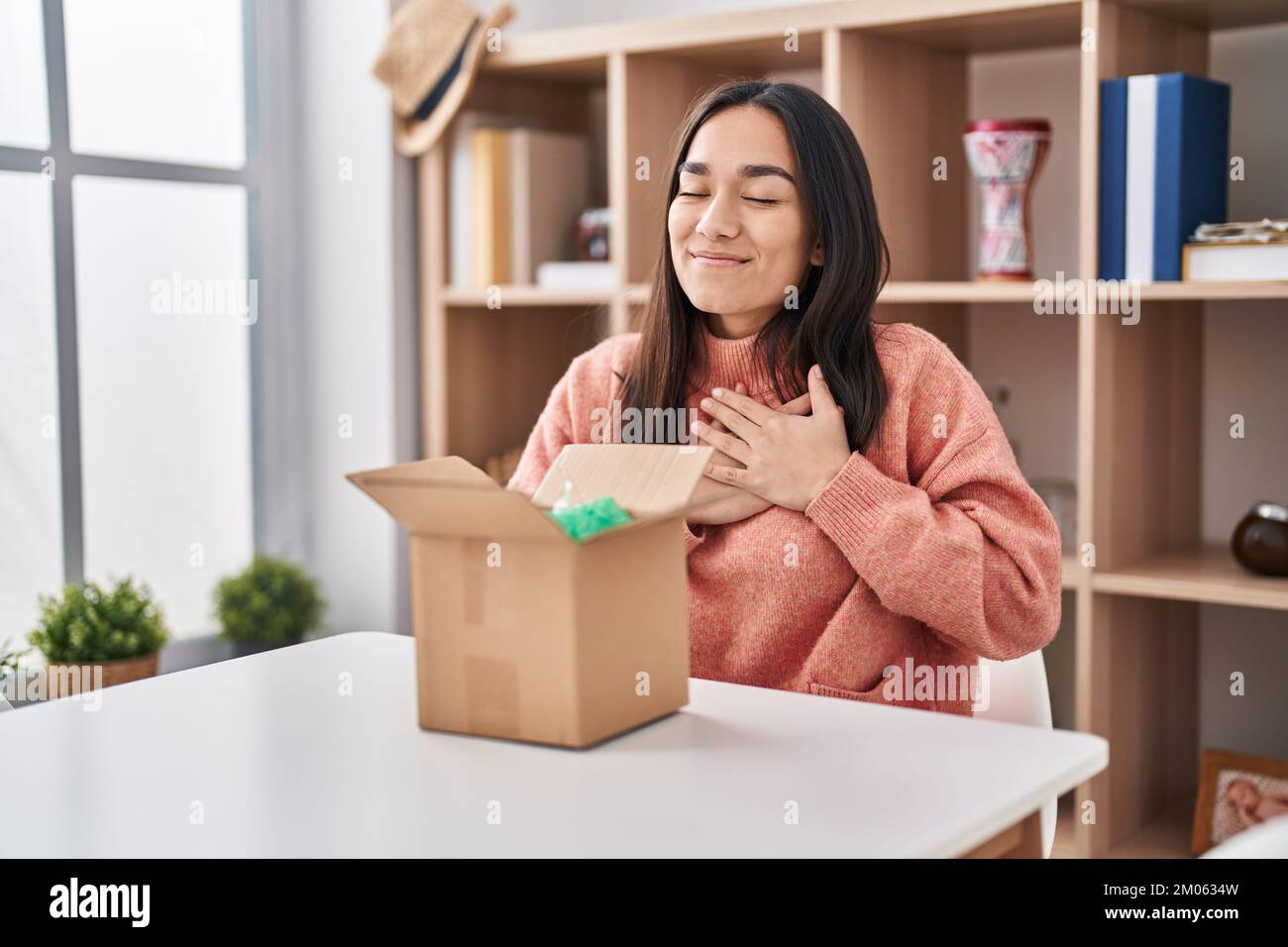 Young south asian woman opening cardboard box smiling with hands on ...