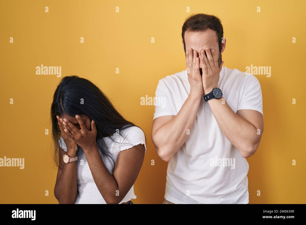Interracial Couple Standing Over Yellow Background With Sad Expression