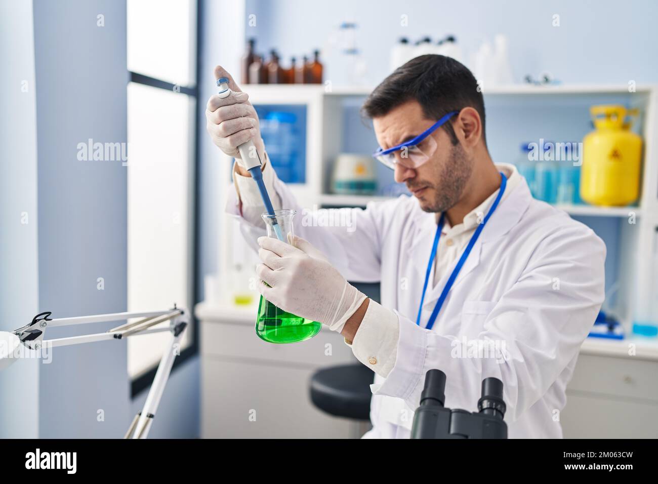 Young hispanic man scientist measuring liquid using pipette at ...