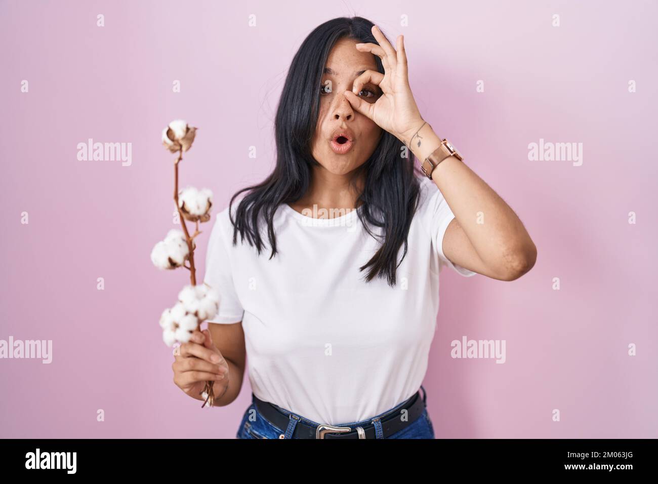 Brunette woman standing over pink background doing ok gesture shocked ...