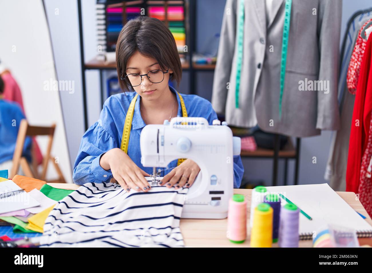 Adorable hispanic girl tailor using sewing machine at clothing factory ...