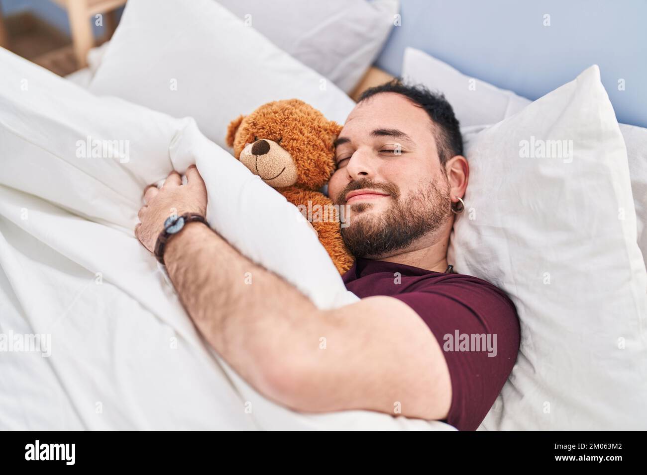 Young Hispanic Man Hugging Teddy Bear Lying On Bed Sleeping At Bedroom