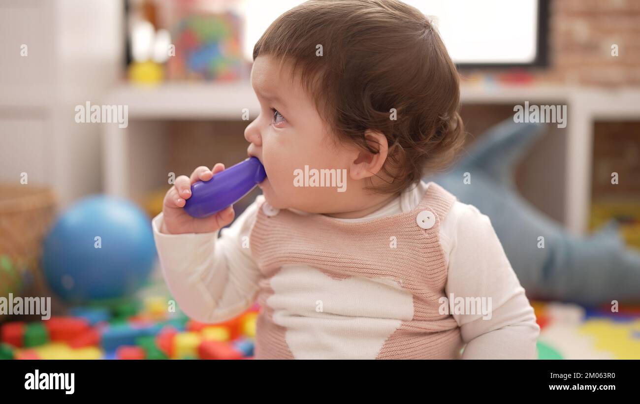 Adorable toddler bitting plastic food toy sitting on floor at ...