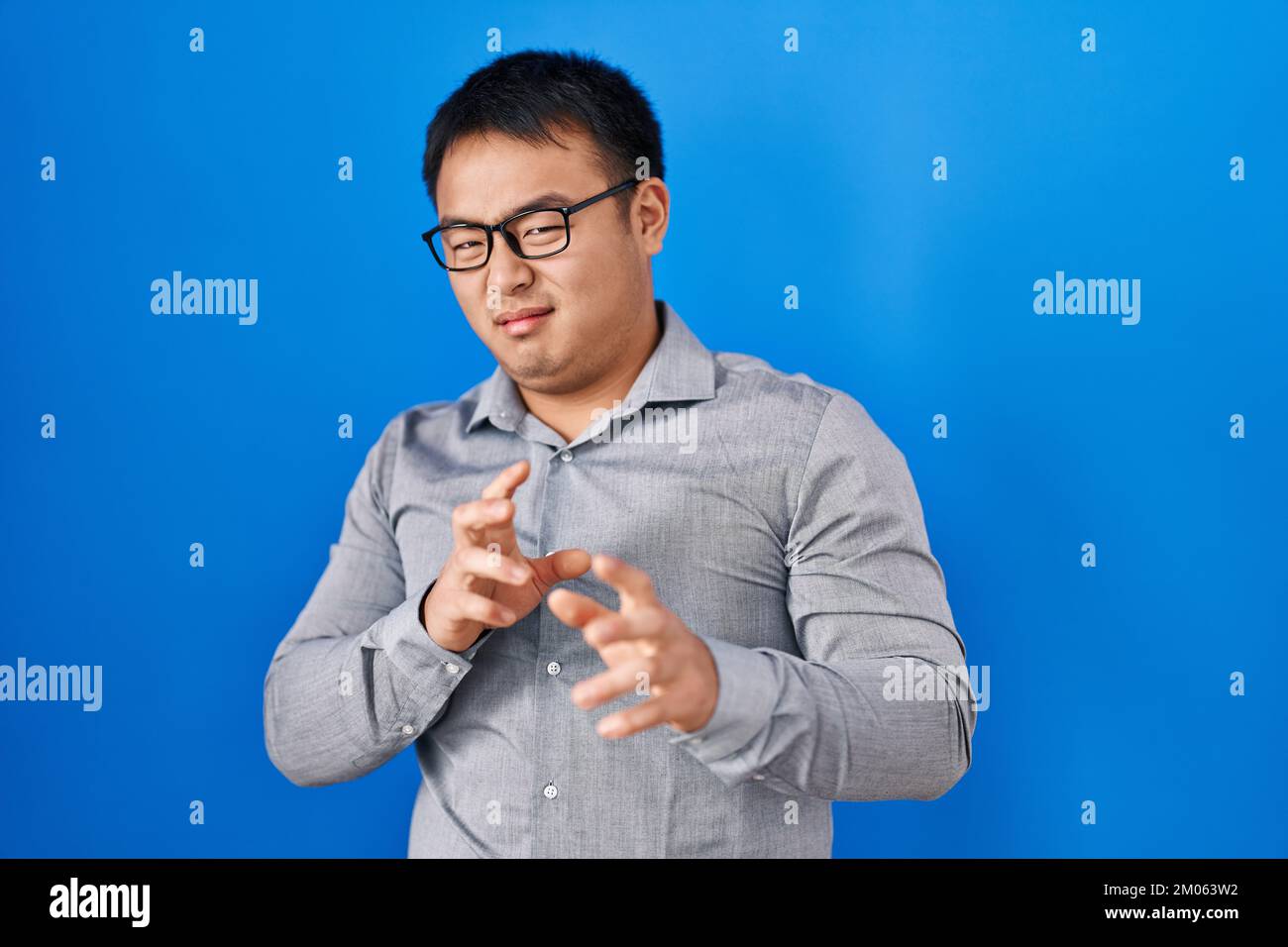 Young chinese man standing over blue background disgusted expression ...