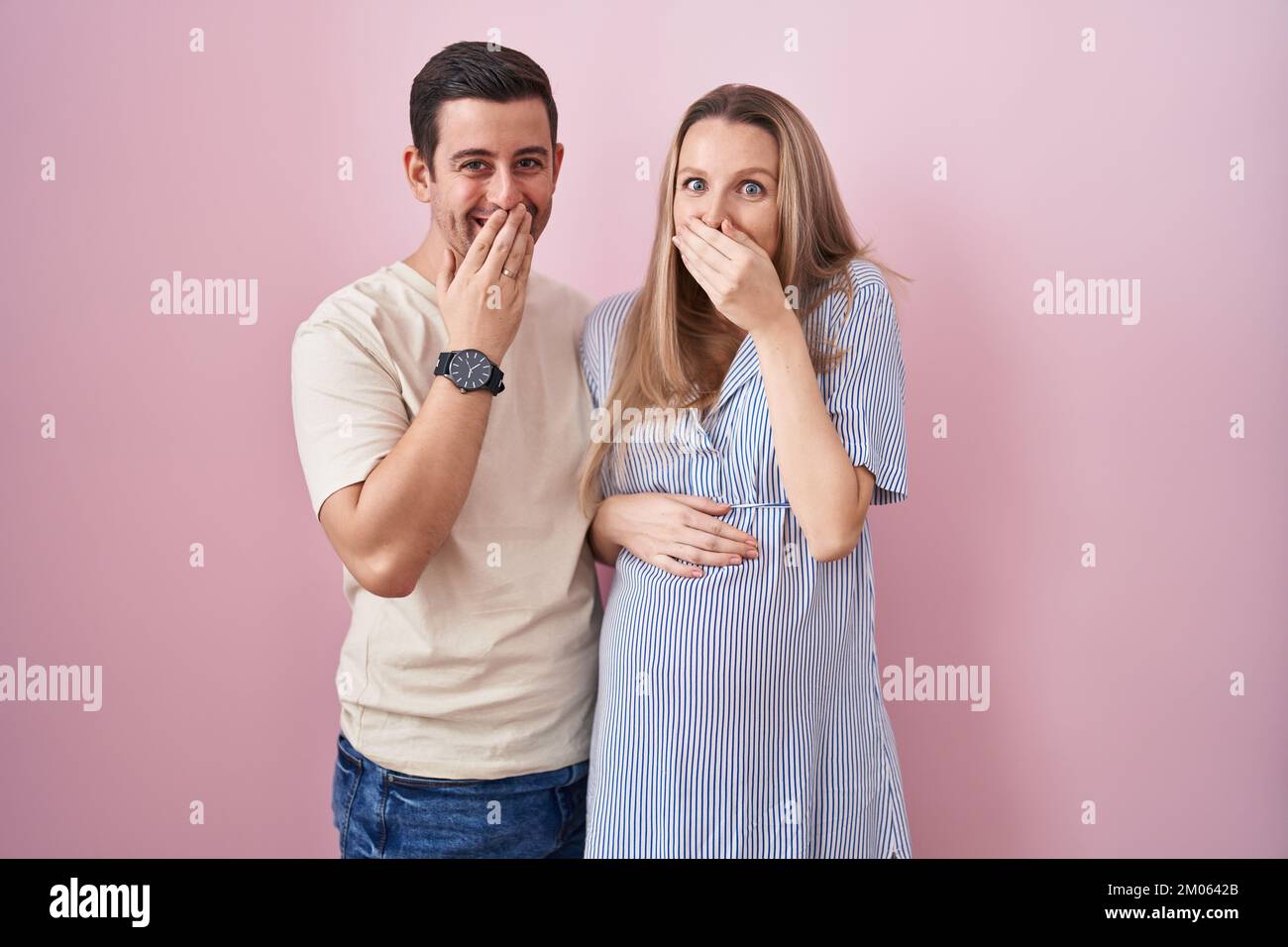 Young couple expecting a baby standing over pink background laughing ...
