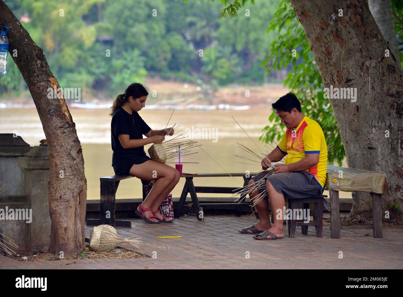 A local man teaching basket weaving to a western tourist by the Mekong ...