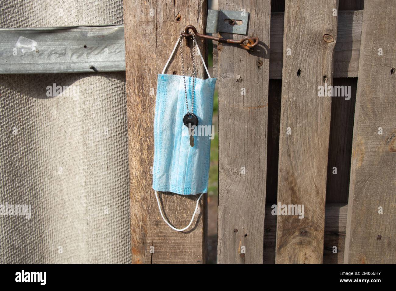 medical mask hanging on a hook and a door key on an old wooden gate in ...