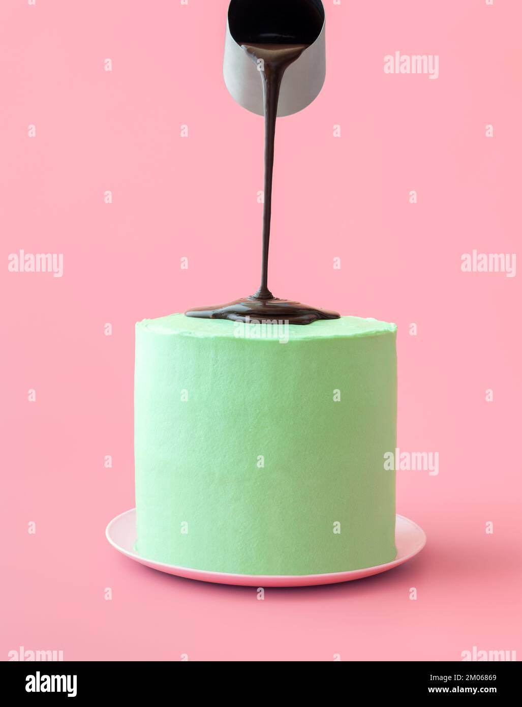 Pouring dark chocolate over frosted cake, minimalist on a pink ...
