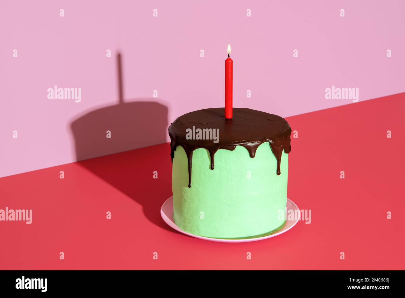 Birthday cake with one lit candle minimalist on a vibrant colored table ...