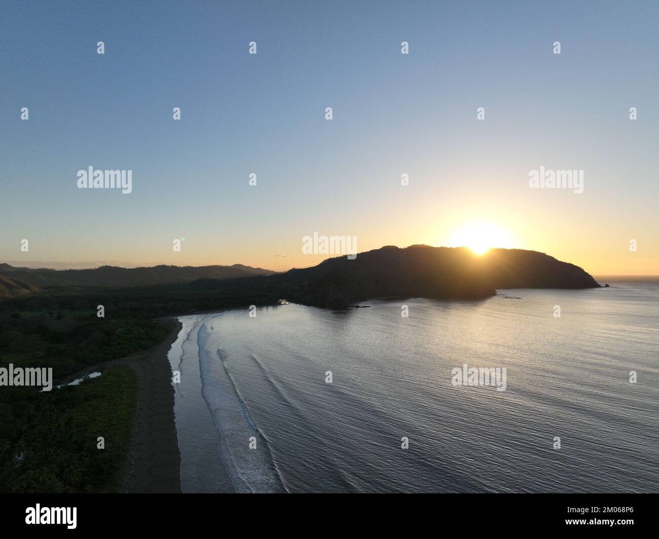 a Sunrise over the ocean with the sun peeking over the mountains in ...