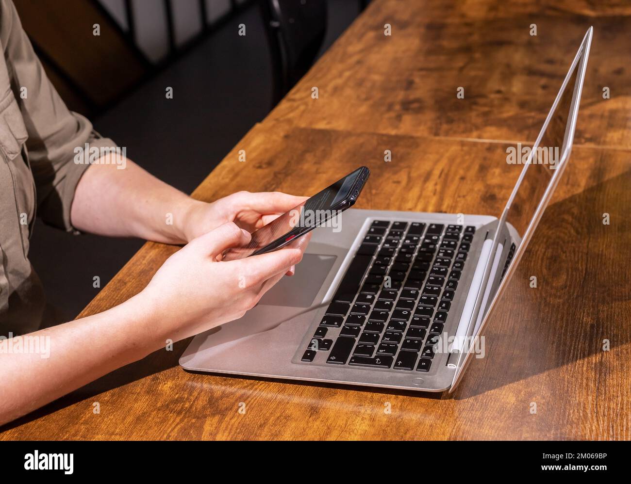 Hand holding mobile phone, sitting at wood desk with laptop computer ...