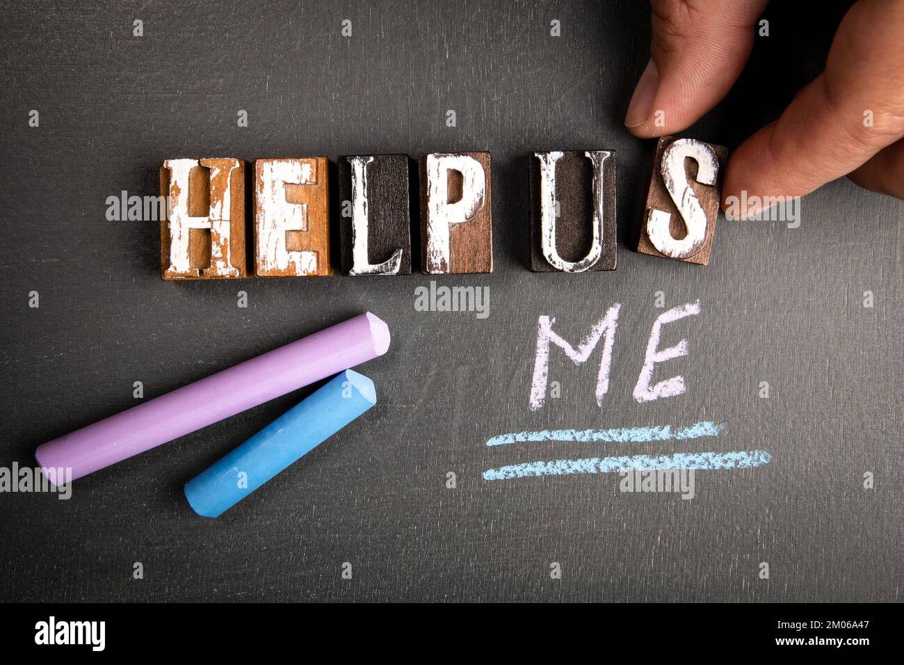 Help Us and Help Me concept. Wooden letters and colored pieces of chalk ...