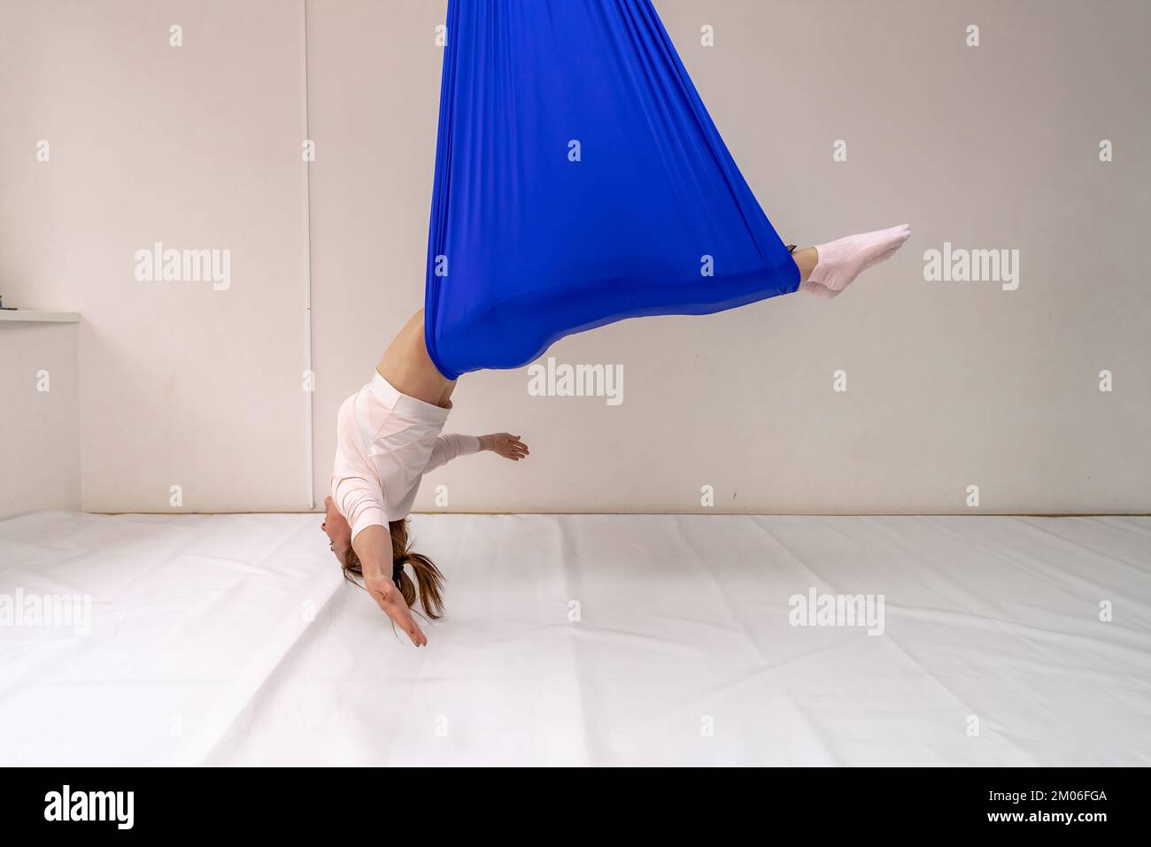 A young woman poses while doing anti-gravity aerial yoga in a blue ...