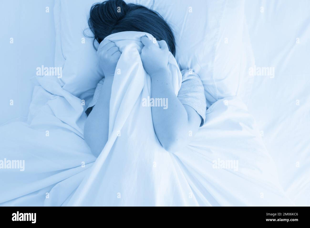 Woman hiding her face under a blanket in bed Stock Photo - Alamy
