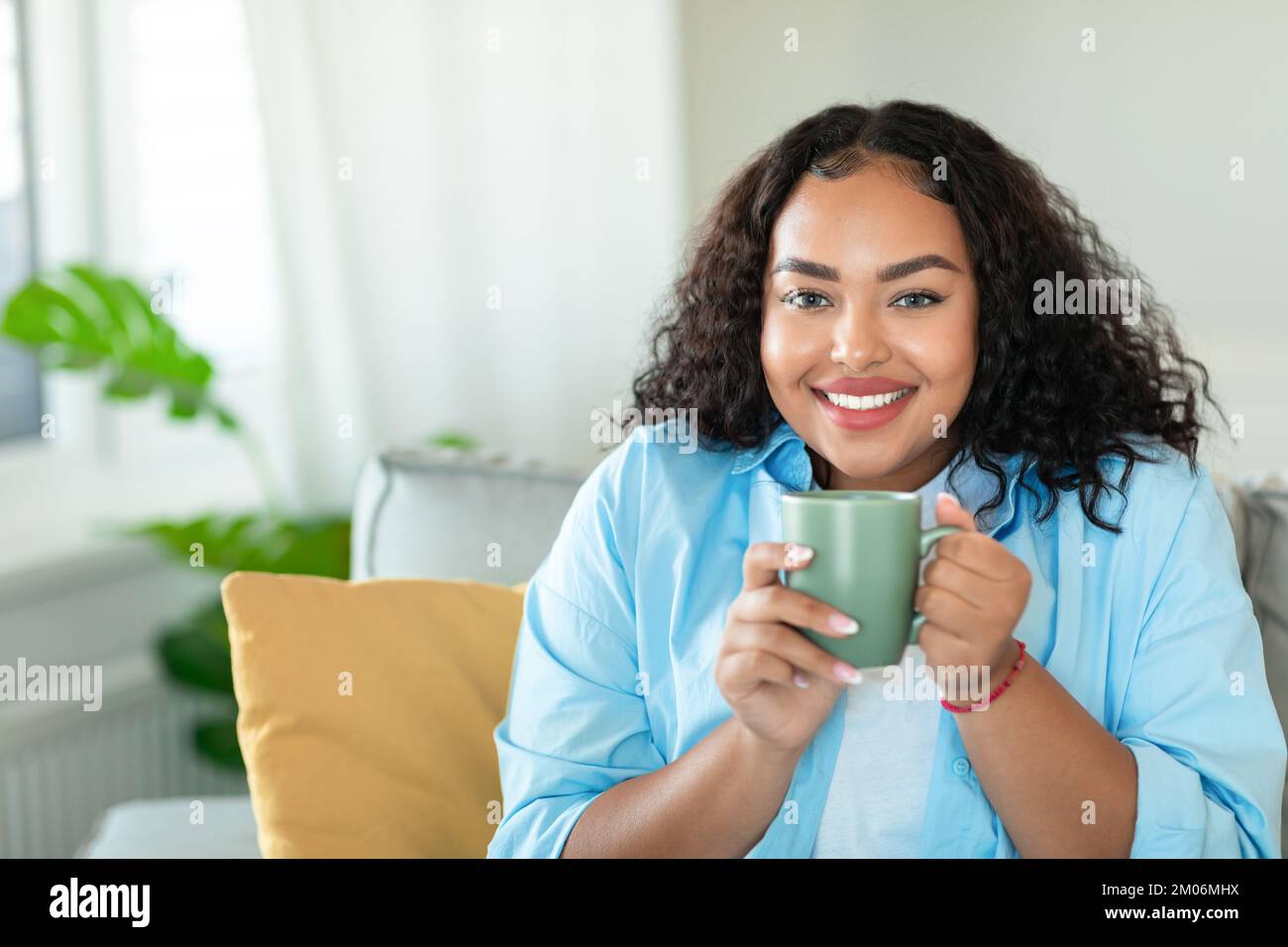 Domestic leisure. Happy black plus size lady drinking coffee at home ...
