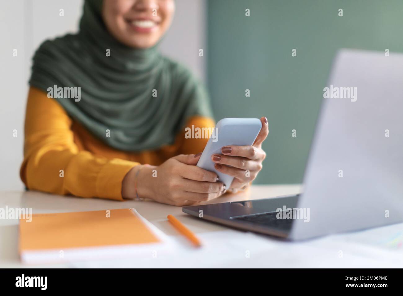 Muslim Woman In Hijab Using Mobile Phone While Sitting At Desk In ...