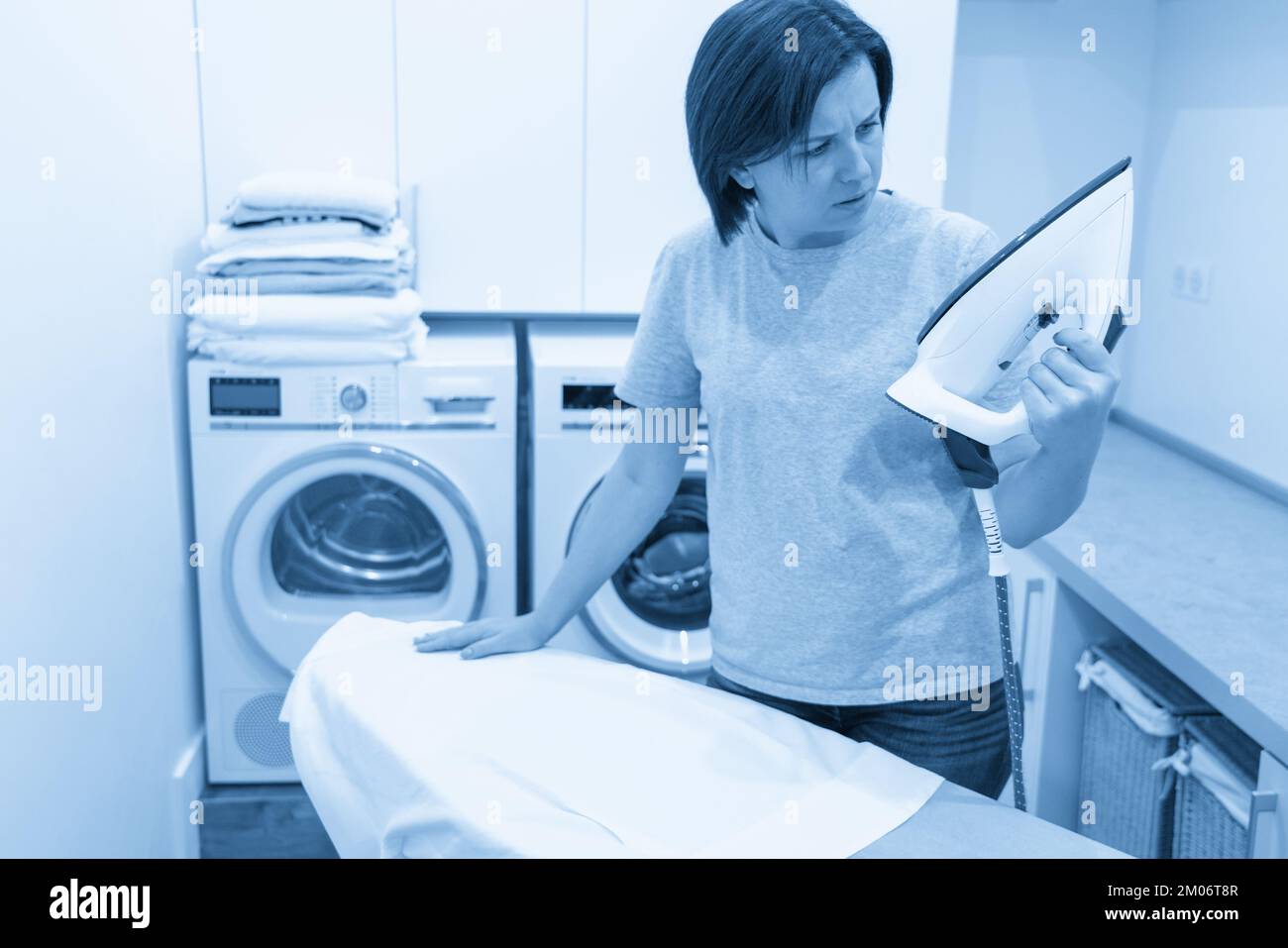 Woman looking with surprise at bottom of broken iron in laundry room ...