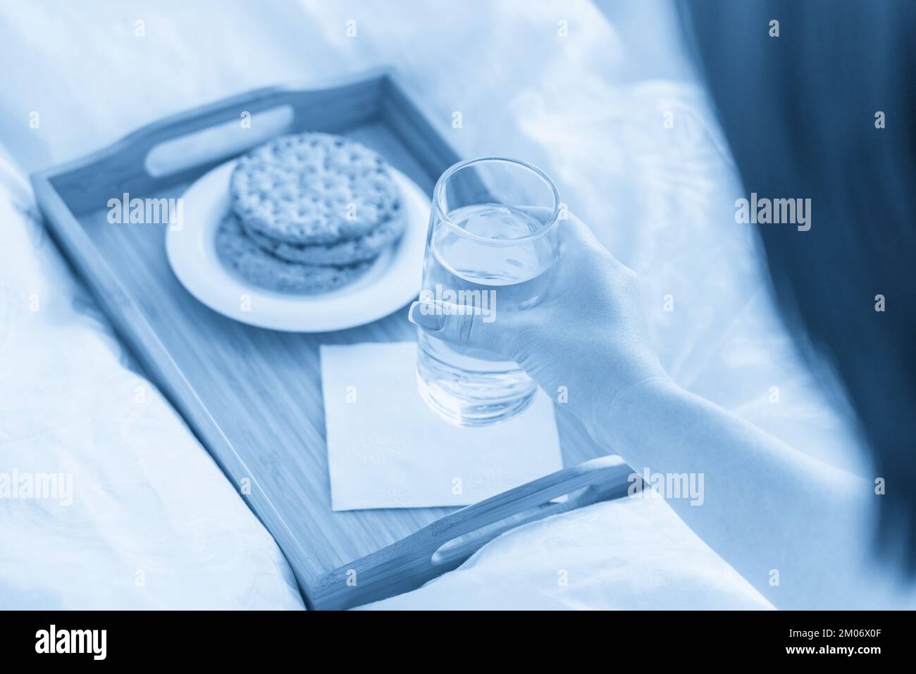 Female hand holding glass of water over tray with crackers on bed Stock ...