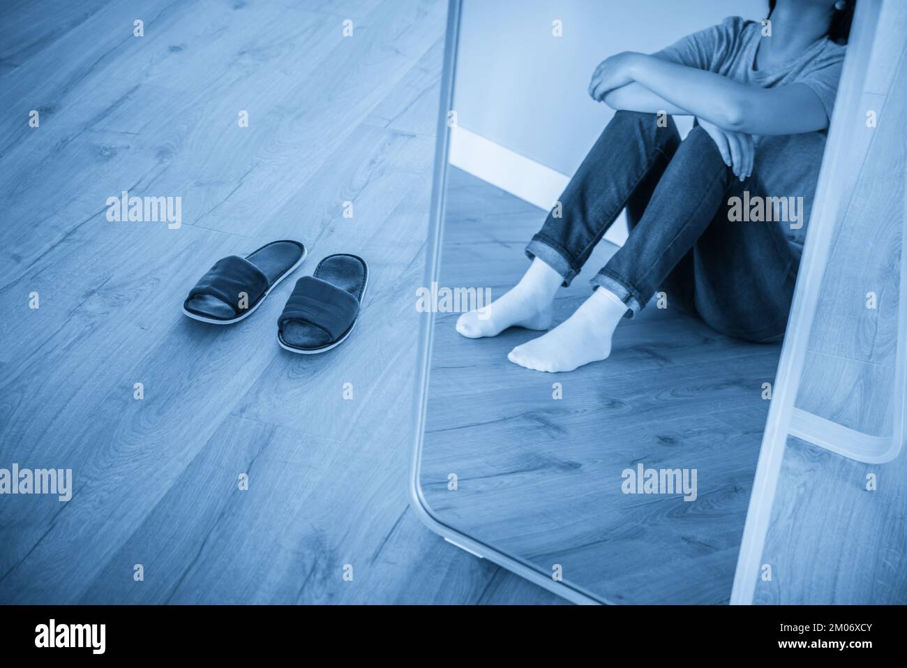 Reflection in mirrow of a sad woman sitting on a floor alone in empty ...