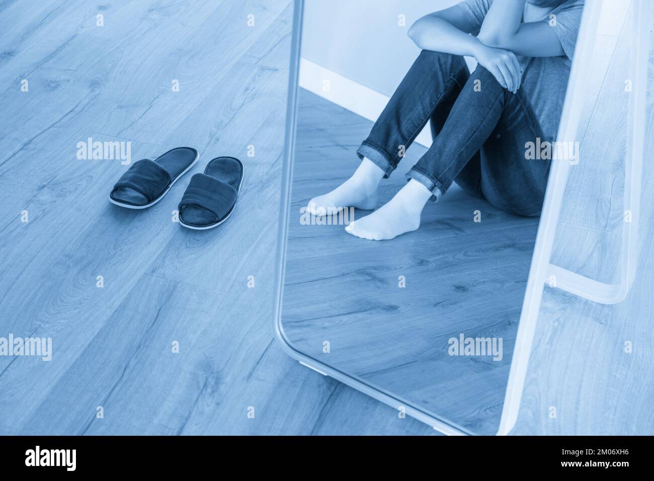 Reflection in mirrow of a sad woman sitting on a floor alone in empty ...