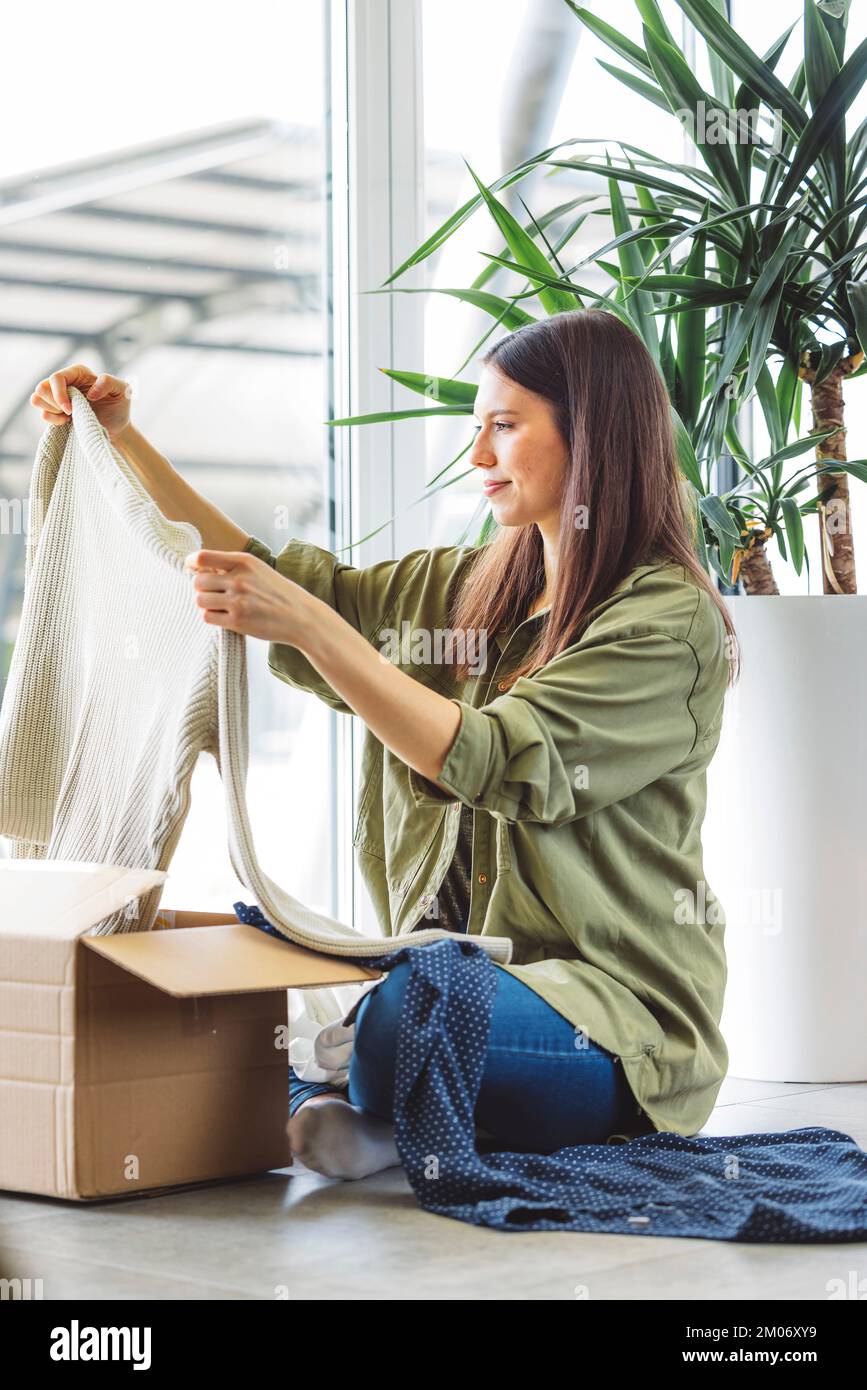Vertical photo of a woman looking trough the clothes she bought online ...