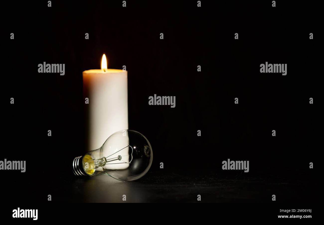 Burning candle near a switched off light bulb in dark home. Blackout ...