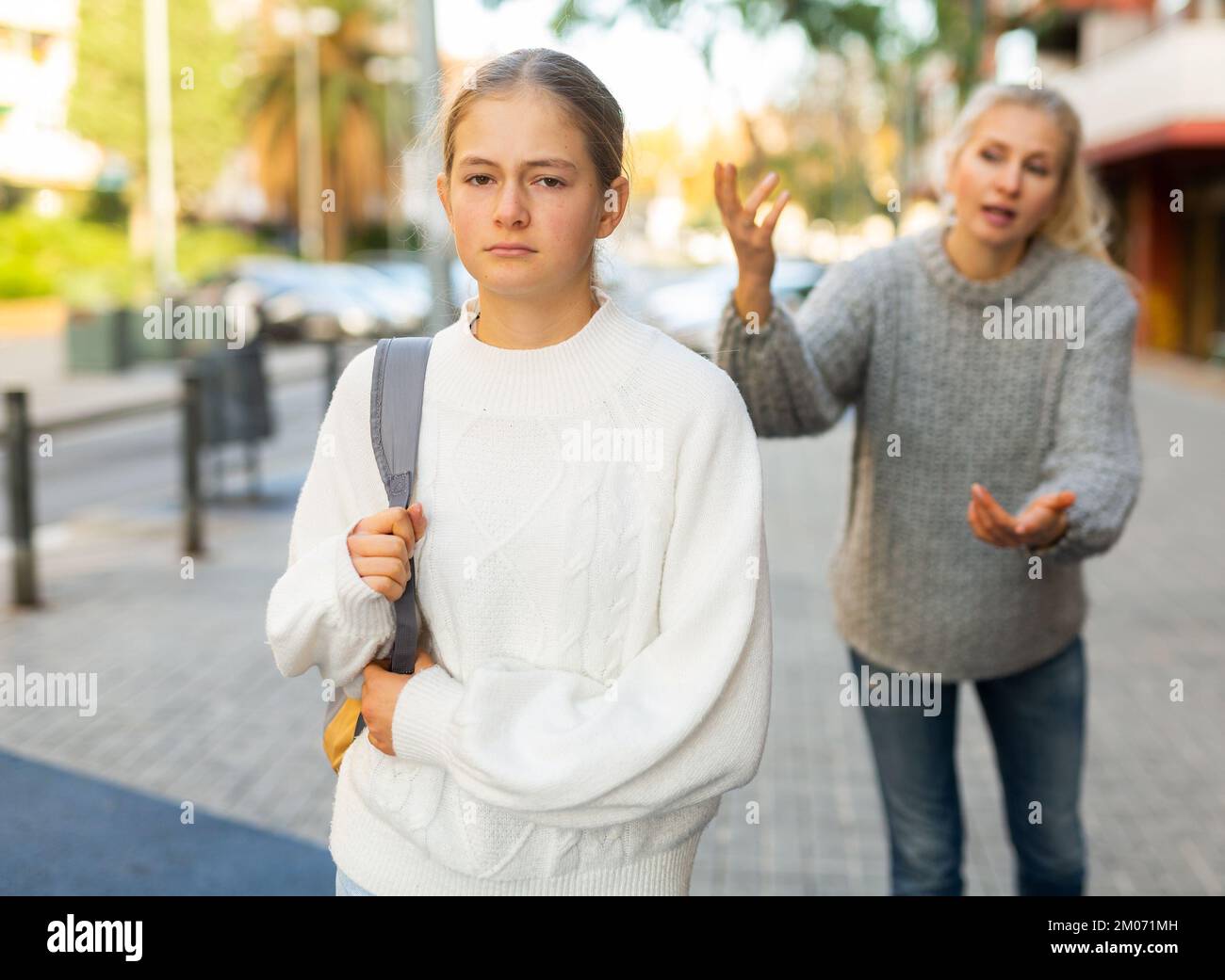 Upset teen girl walking on city street with worried mother reproaching ...