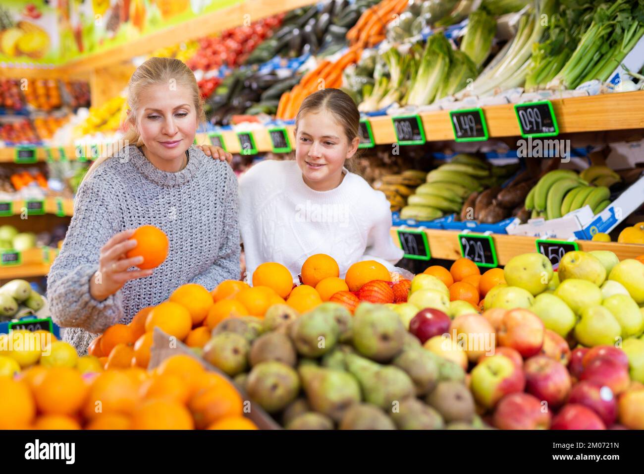 Portrait of teenage girl and mother who buying fresh oranges at grocery ...