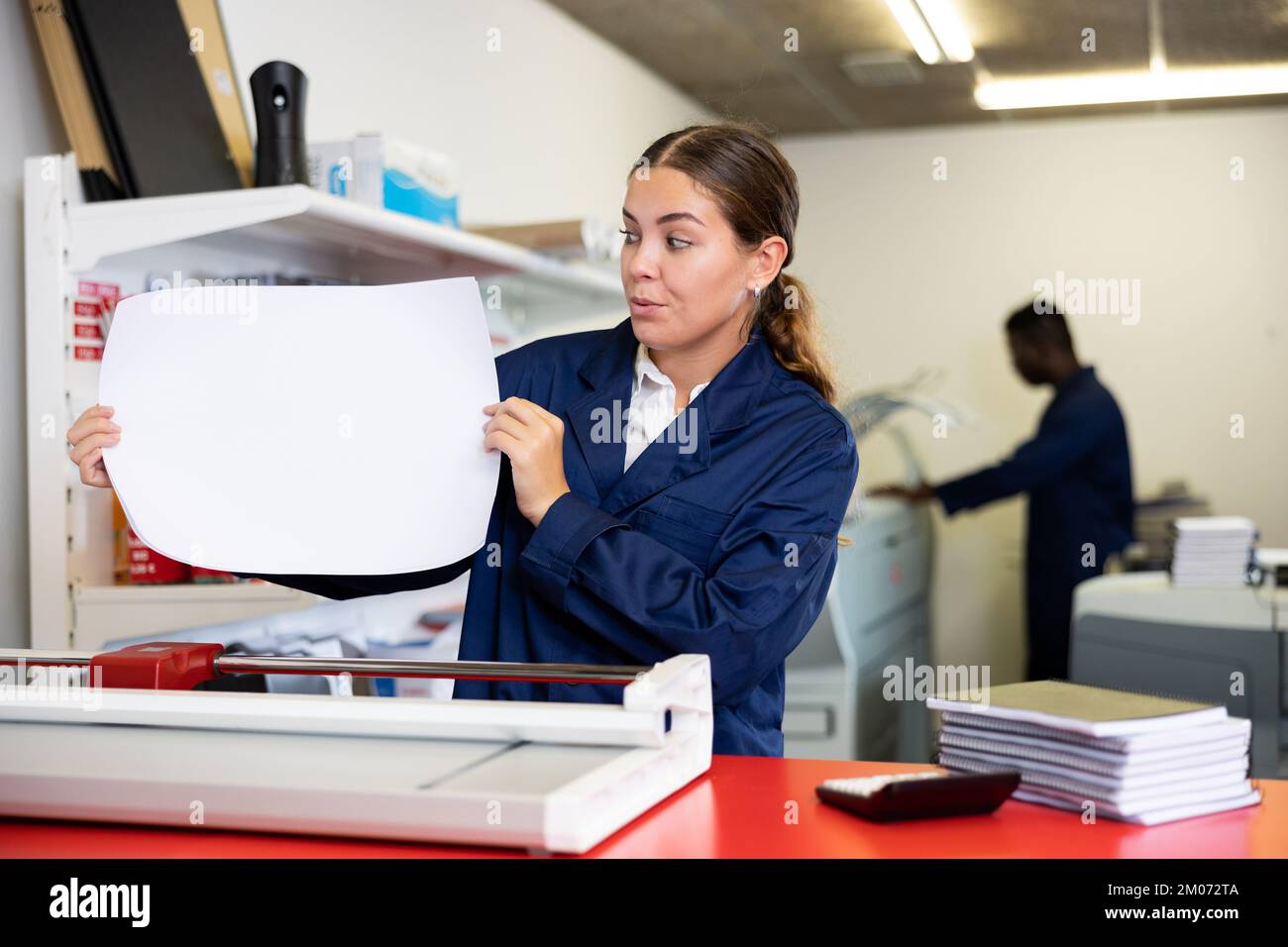 Attentive young female in a blue uniform verifying printed sheet during ...