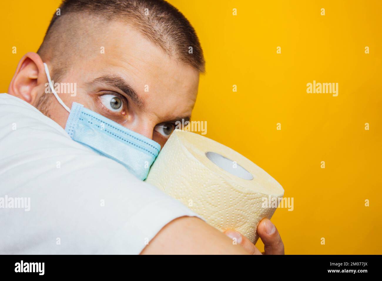A young man in a medical mask holds rolls of toilet paper, shows a ...