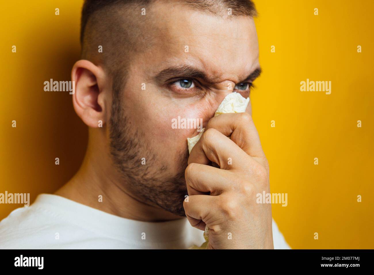 A young guy sick with a virus sneezes into toilet paper that he holds ...