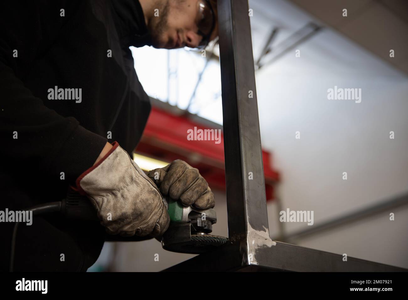 A worker uses a sander on a metal bar in a workshop Stock Photo - Alamy
