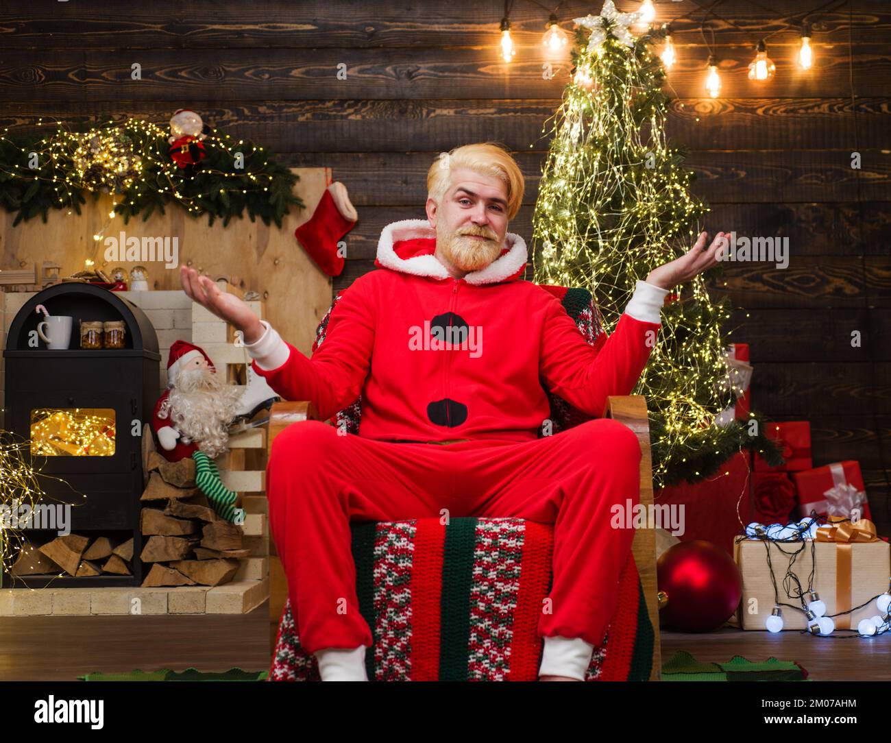 Santa Claus sits in chair at room near fireplace and New year tree ...