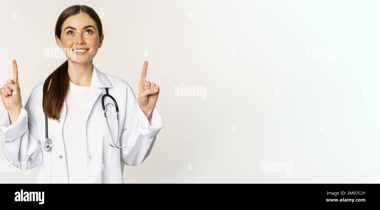 Happy beautiful doctor, female physician pointing fingers up, showing ...
