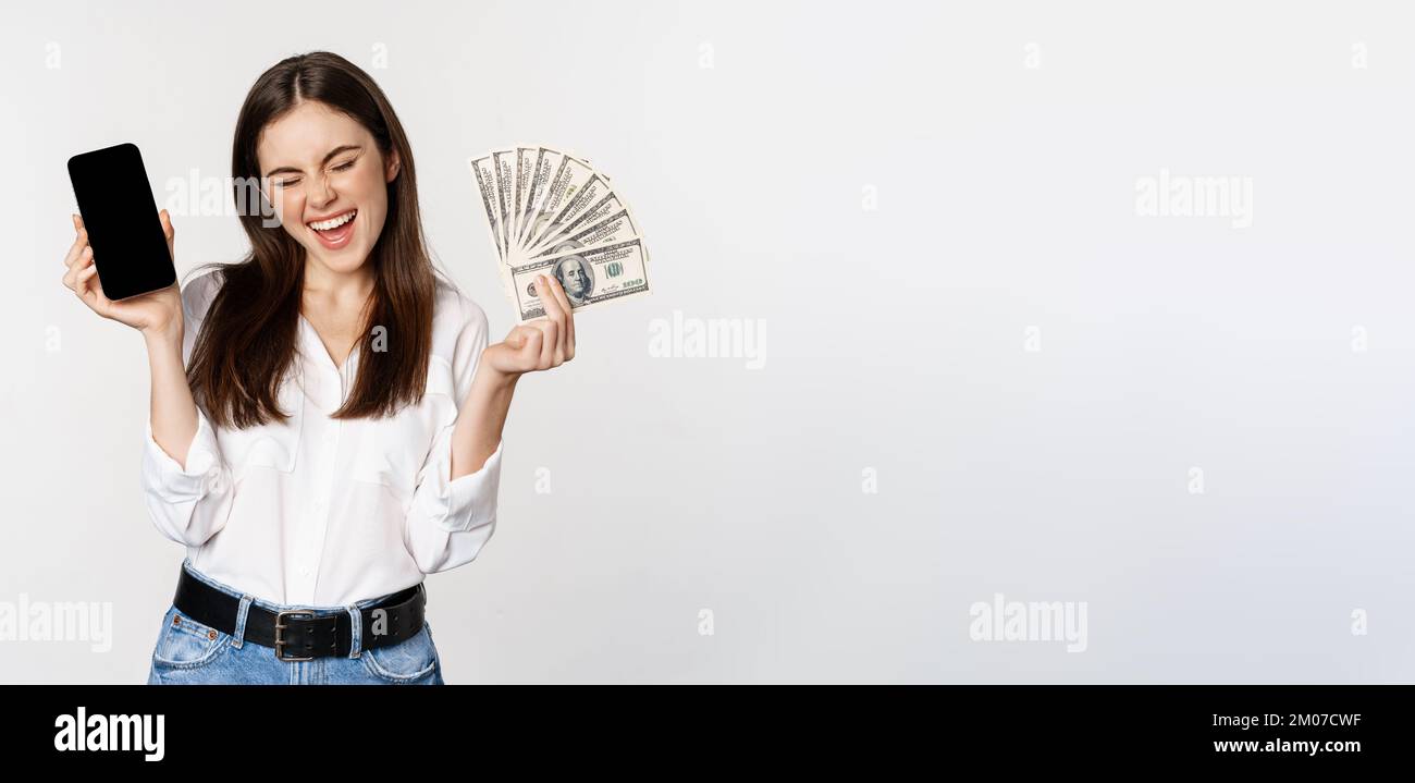 Enthusiastic young woman winning money, showing smartphone app ...