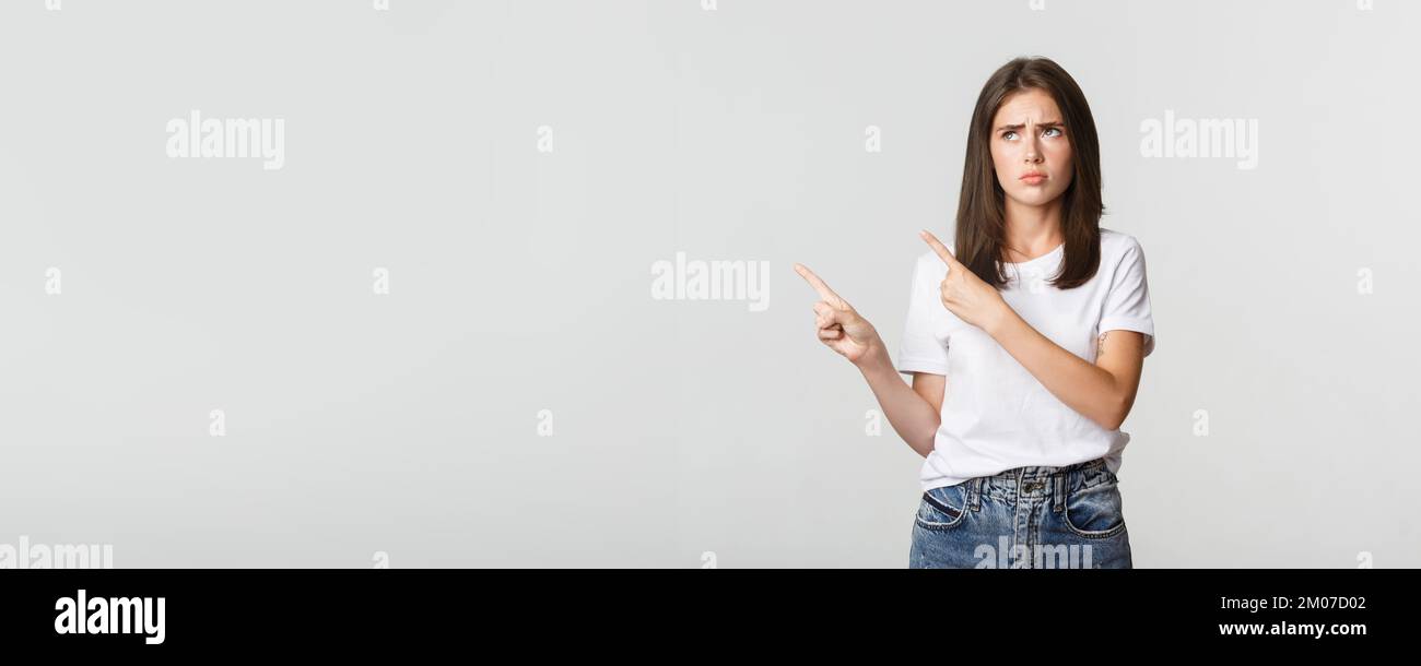 Upset cute girl pointing upper left corner, express regret Stock Photo ...