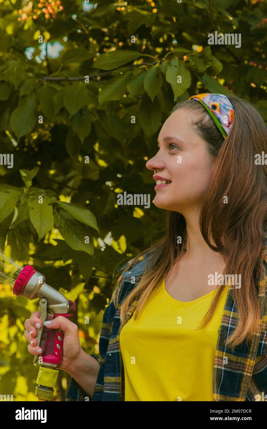 young pretty girl having fun in the garden watering plants with a hose ...