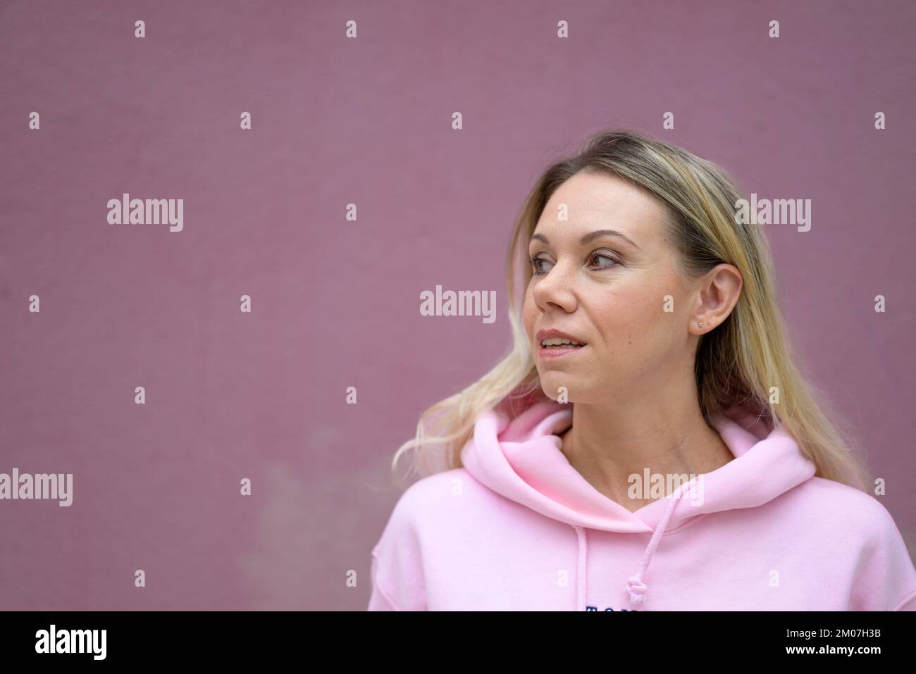 Gorgeous blonde attractive woman in a pink hoodie in front of a pink ...