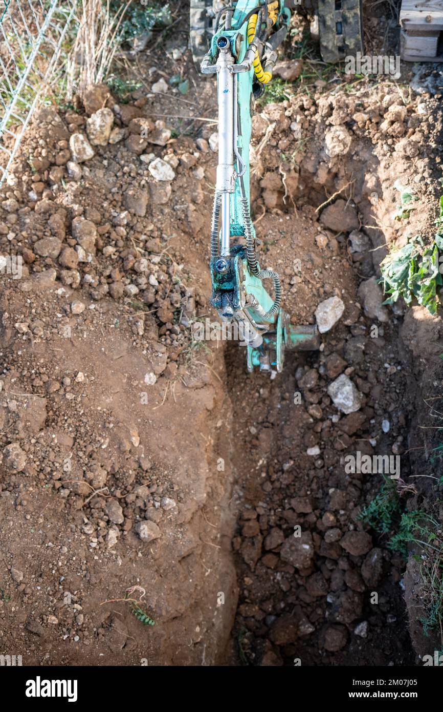 Mini excavator digs a trench to lay pipes. Close up of an excavator digging a deep trench. An ...
