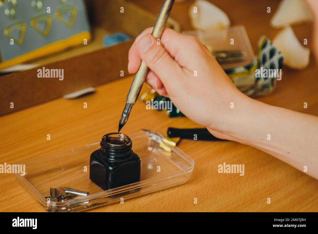 female hand dipping ink pen into inkwell. stationery on wooden desk ...
