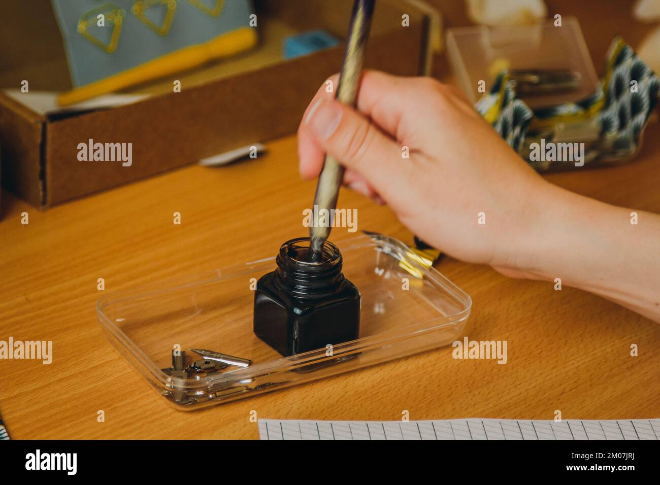 female hand dipping ink pen into inkwell. stationery on wooden desk ...