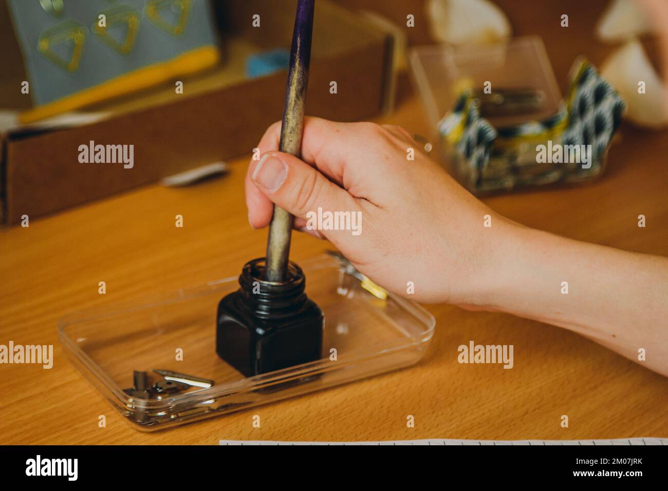 female hand dipping ink pen into inkwell. stationery on wooden desk ...