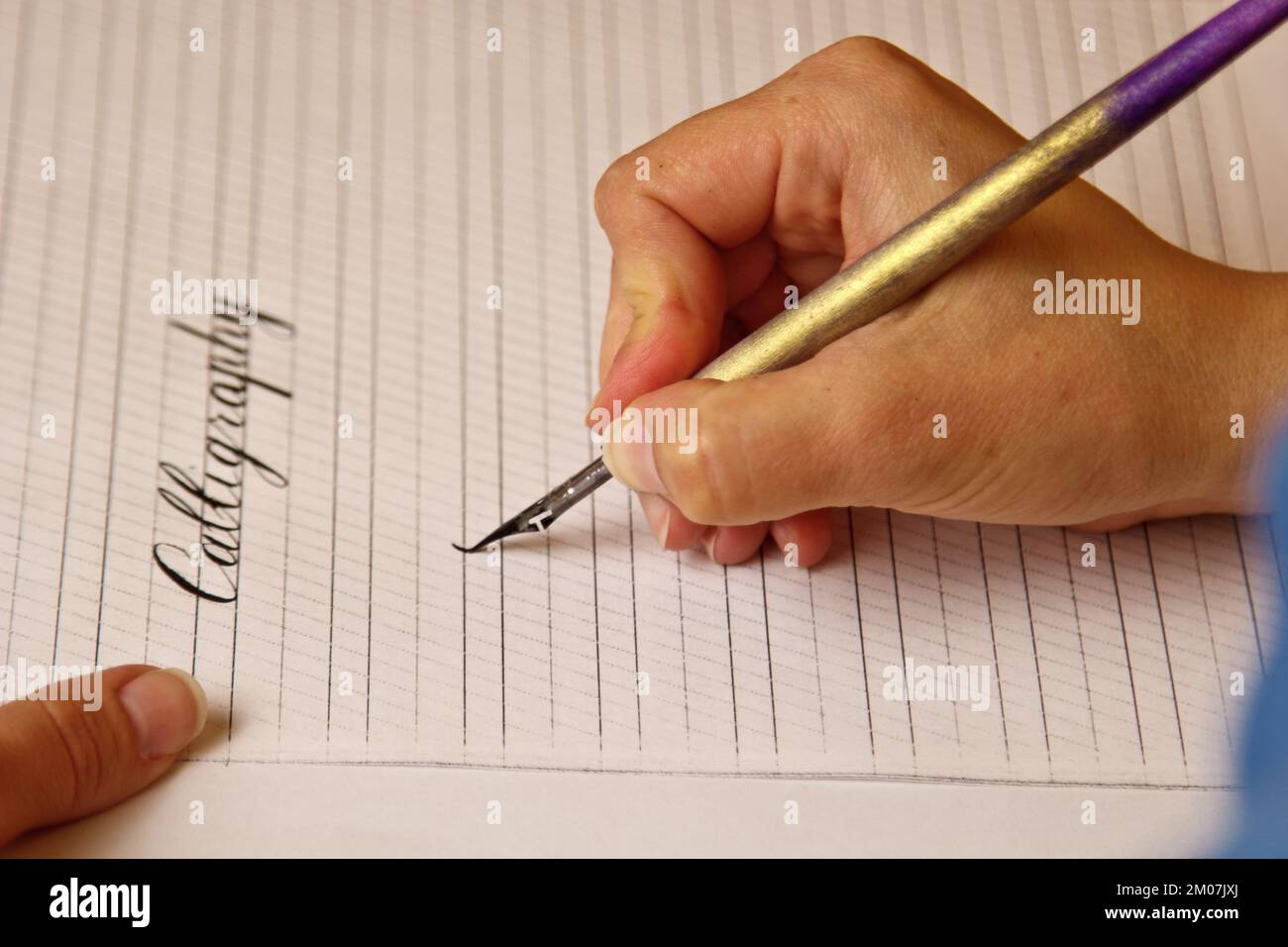 female hand writes with the inky pen the word calligraphy on a paper ...