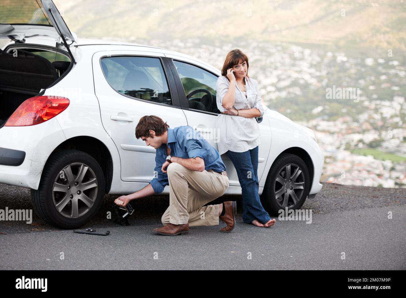 Calling roadside assist. Young couple stuck on a hillside road after ...